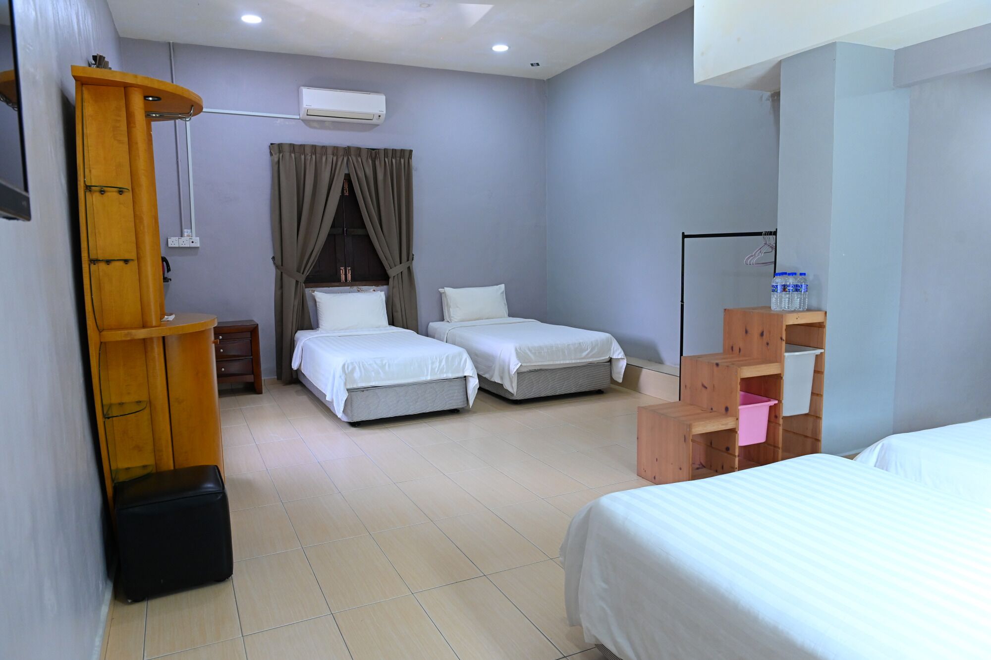 Quarto de hotel com duas camas, um guarda-roupa, uma mesa de trabalho, uma cadeira e um dispensador de água.