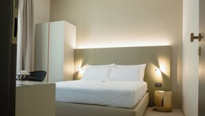 Quarto de hotel com cama, mesa de cabeceira, cadeira e uma pequena mesa com abajur.