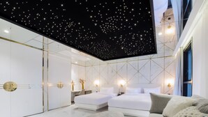 Quarto de hotel moderno com teto estrelado, uma cama grande, um sofá e uma mesa de mármore.