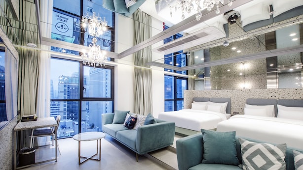 Quarto de hotel moderno com uma cama grande, dois sofás, uma mesinha e vista para a cidade através de amplas janelas.