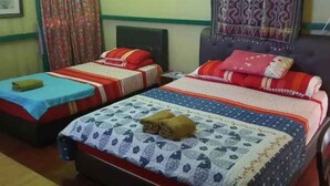 Quarto com duas camas de solteiro, cada uma com colcha listrada em vermelho e branco e almofadas combinando. Há uma colcha azul na cama da esquerda e uma colcha estampada na cama da direita. Uma bolsa marrom está colocada na cama da esquerda.