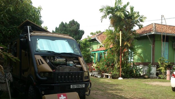 Veículo militar estacionado numa área gramada, com uma casa ao fundo.