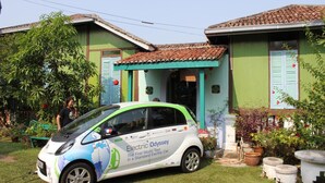 Um pequeno carro elétrico estacionado em frente a uma casa com telhado de azulejos e paredes verdes.