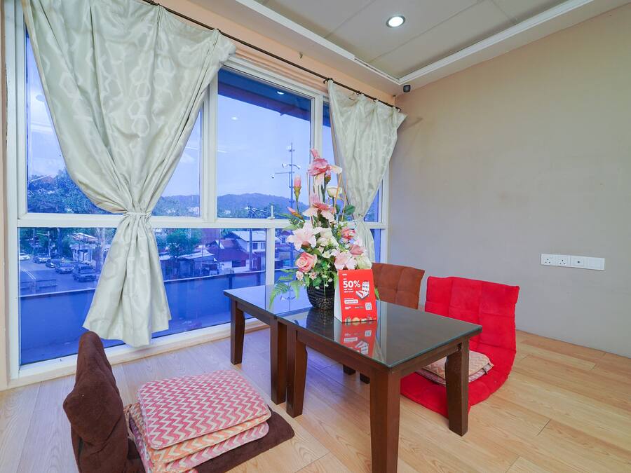 Um quarto com uma mesa de jantar, cadeiras, um sofá vermelho, uma janela com cortinas e um vaso com flores.