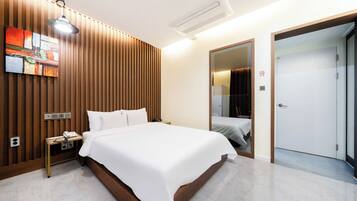 Quarto de hotel moderno com uma cama grande, painel de parede de madeira, um quadro, mesa de cabeceira com telefone e porta para o banheiro.
