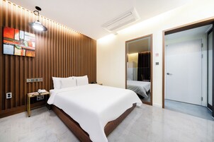 Quarto de hotel moderno com uma cama grande, painel de parede de madeira, um quadro, mesa de cabeceira com telefone e porta para o banheiro.