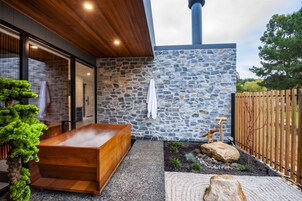 Uma área de spa moderna ao ar livre, com hidromassagem, parede de pedra, deck de madeira e cerca de madeira.