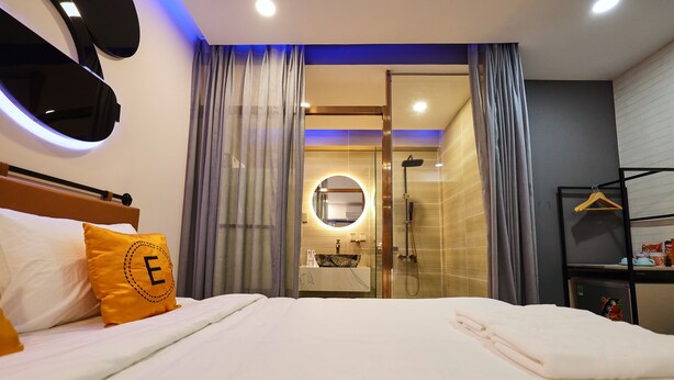 Quarto de hotel com cama, mesa de cabeceira, espelho, chuveiro e guarda-roupa.