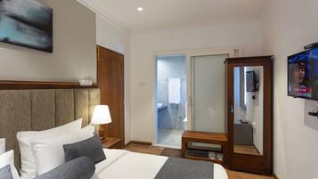 Quarto de hotel com cama, televisão, espelho e porta do banheiro.