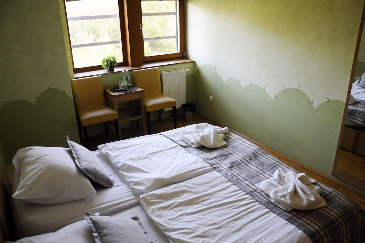 Quarto com duas camas, uma escrivaninha, uma cadeira e um radiador.