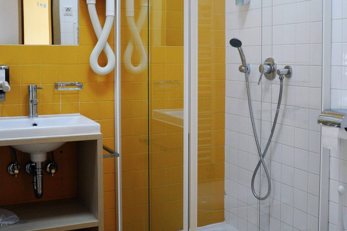Uma casa de banho com chuveiro em cabine de vidro, lavatório com espelho em cima e sanita.