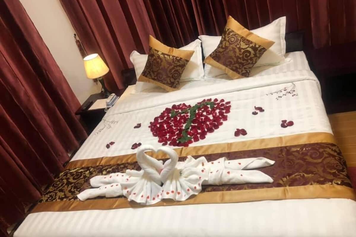 Cama bem arrumada com um arranjo de pétalas de rosas vermelhas em formato de coração e um arranjo de toalha em forma de cisne.