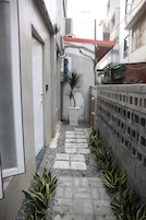 Um beco estreito com caminho de concreto, plantas em vasos e parede de tijolos.