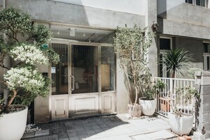 Entrada de um edifício com porta de vidro, plantas em vasos e cerca branca.