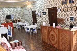 Uma área de recepção com balcão de madeira, cadeiras brancas e parede estampada.