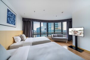 Quarto de hotel com duas camas, televisão, vista para a cidade e design moderno.