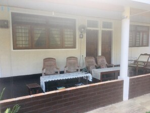 Uma área de estar coberta ao ar livre, com mesa, cadeiras, um ventilador e uma parede de tijolos.
