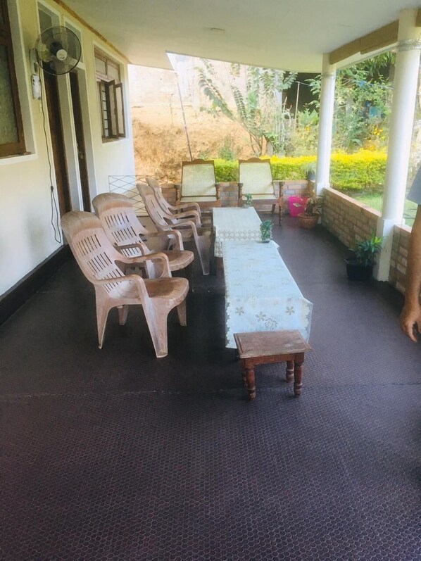 Uma área de estar coberta ao ar livre, com uma mesa comprida e várias cadeiras de plástico.