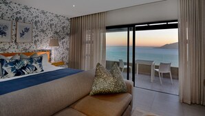 Quarto de hotel com cama, sofá, varanda vista para o mar e área de refeições.