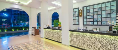 Área de recepção de hotel com piso estampado, balcão de atendimento e vista para o exterior à noite.