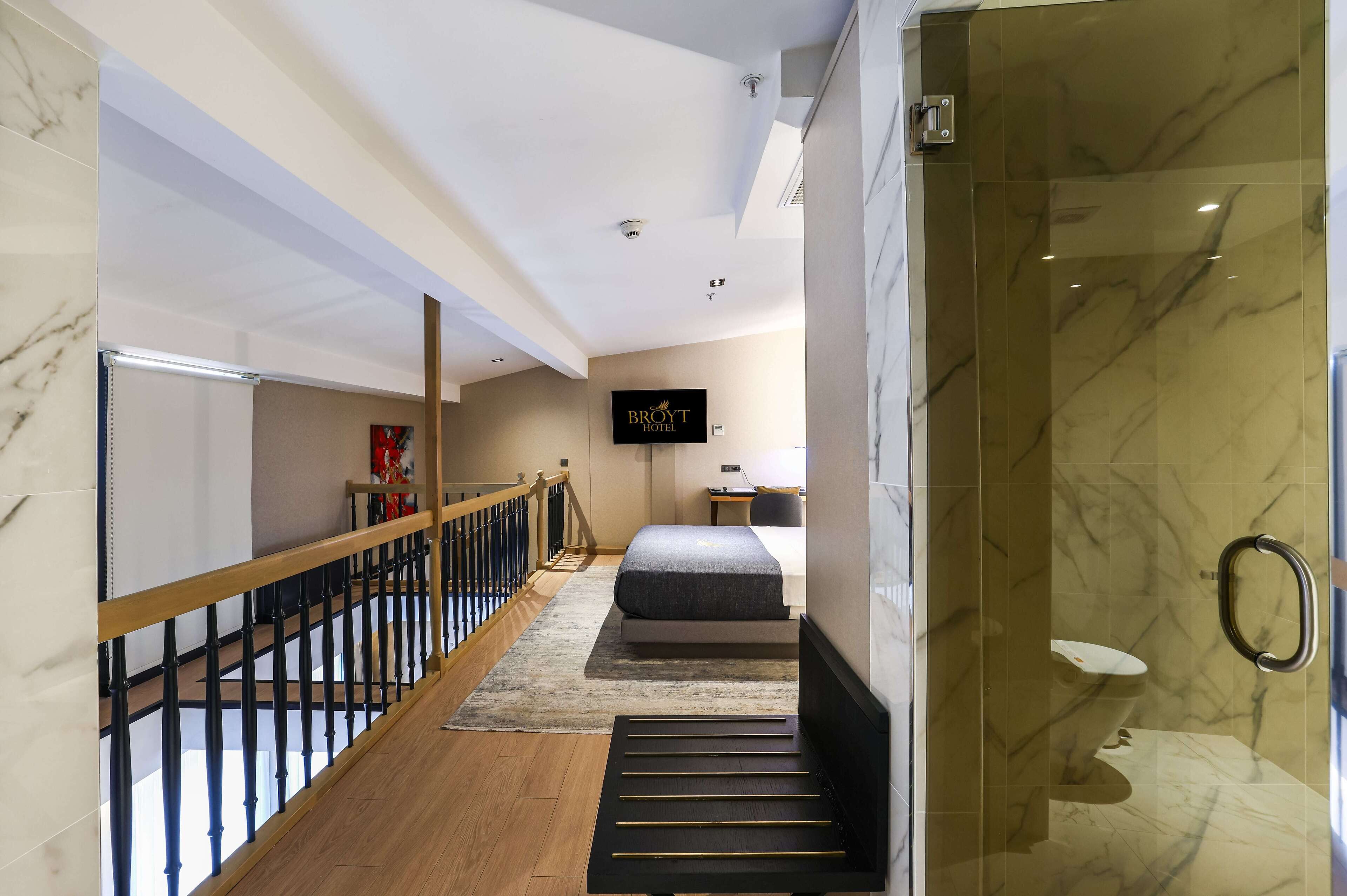 Quarto de hotel com uma cama, escrivaninha, televisão e banheiro com chuveiro de mármore.