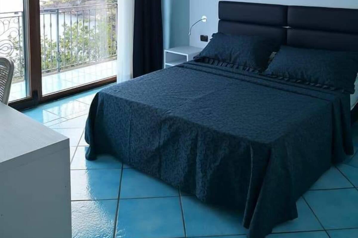 Quarto com cama, escrivaninha, cadeira, janela com cortinas e ar condicionado.