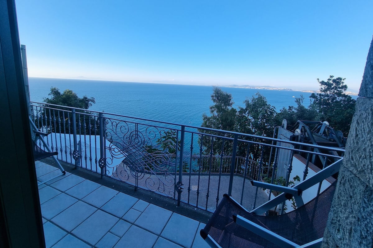 Uma varanda com vista para o mar, uma cadeira e um corrimão.