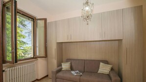 Quarto com sofá marrom, janela com vista, radiador e lustre.