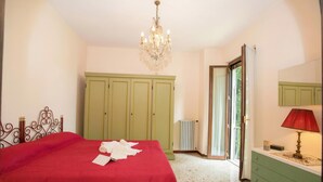 Quarto com cama, lustre, guarda-roupa verde, radiador e janela.