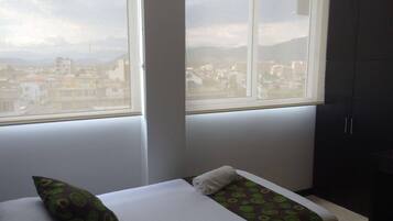 Quarto de hotel com cama, janela vista para a cidade e guarda-roupa escuro.