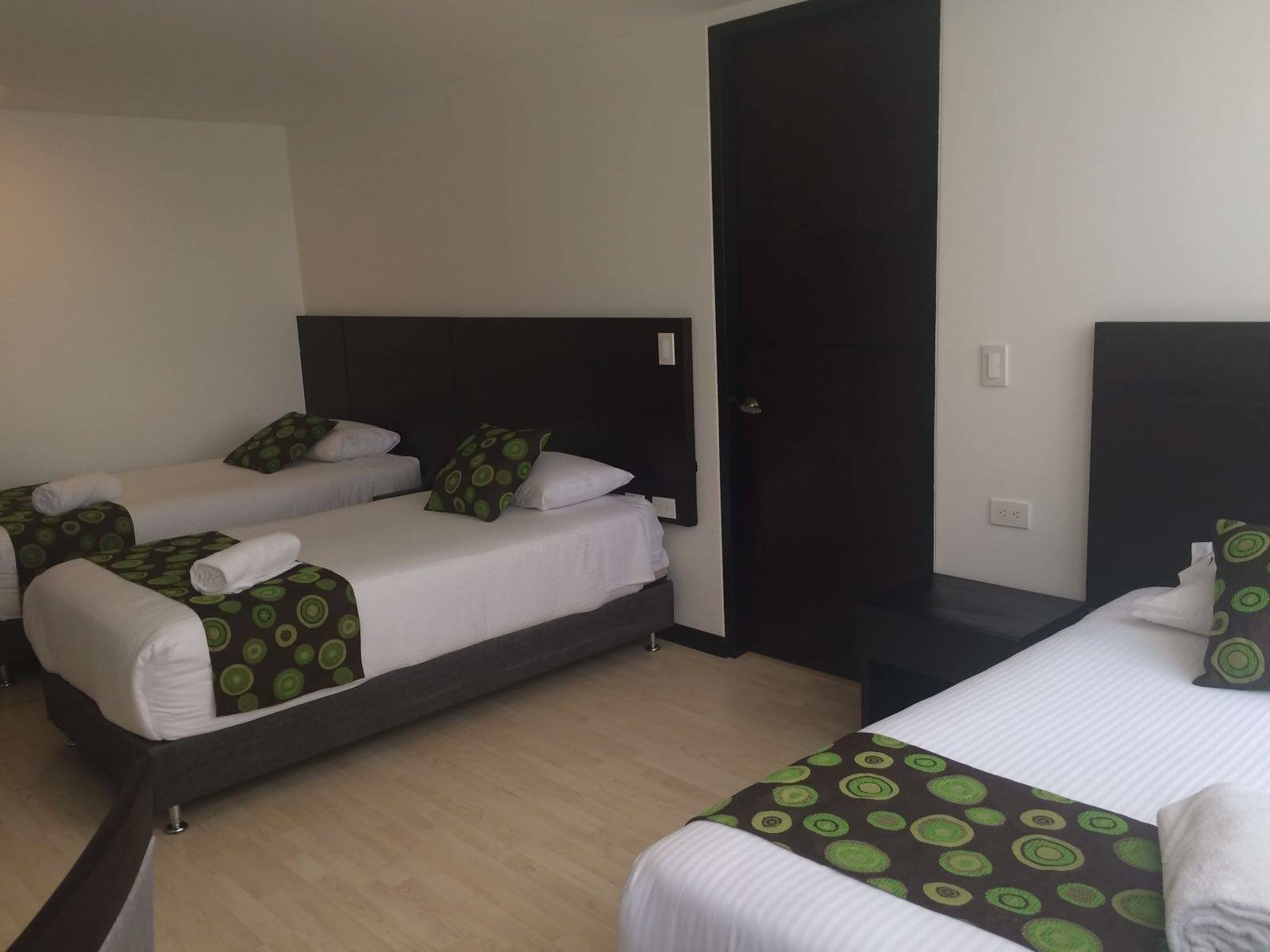 Quarto de hotel com duas camas de solteiro, cada uma com cabeceira escura, roupa de cama branca e edredons estampados em verde.