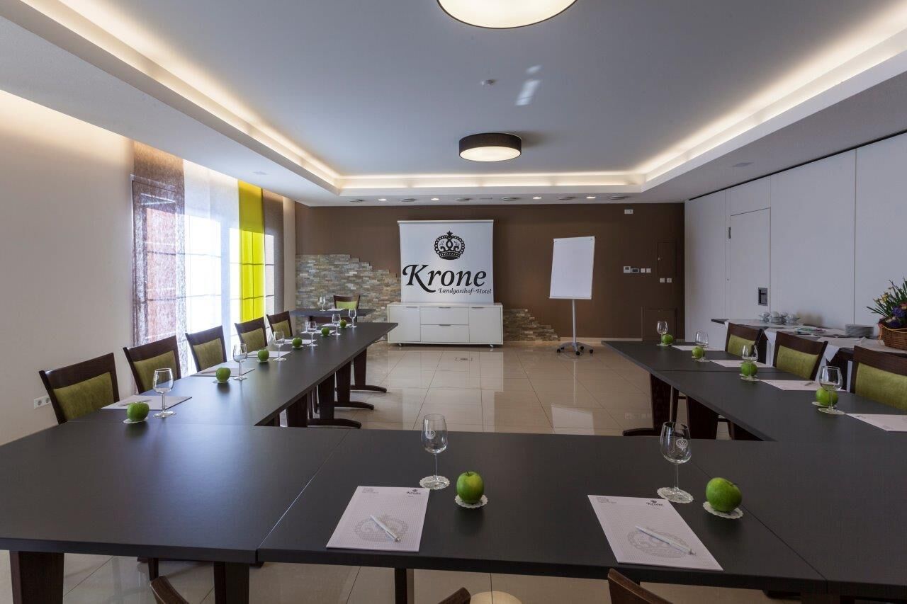Uma sala de conferências com uma mesa comprida, cadeiras e um banner com a inscrição 'Krone'.