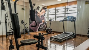Academia com diversos equipamentos de exercício, incluindo esteira, aparelhos de musculação e um espelho refletindo o interior.