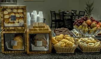 Um buffet de café da manhã com diversos pães, doces e frutas.