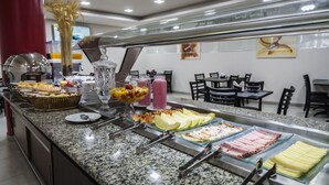 Buffet com diversos tipos de comida e área de refeições com mesas e cadeiras.
