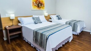 Quarto de hotel com duas camas, uma mesa de cabeceira, um abajur e um quadro na parede.