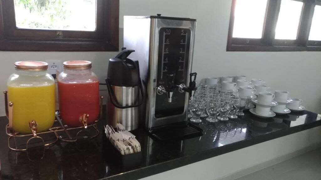 Uma bancada de cozinha com dois potes de vidro de suco, uma cafeteira e uma fileira de xícaras e pires brancos.