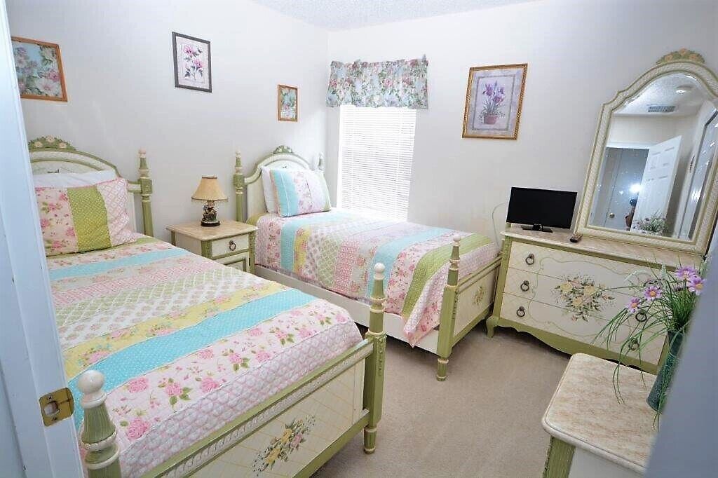 Quarto com duas camas, cômoda, televisão e espelho.
