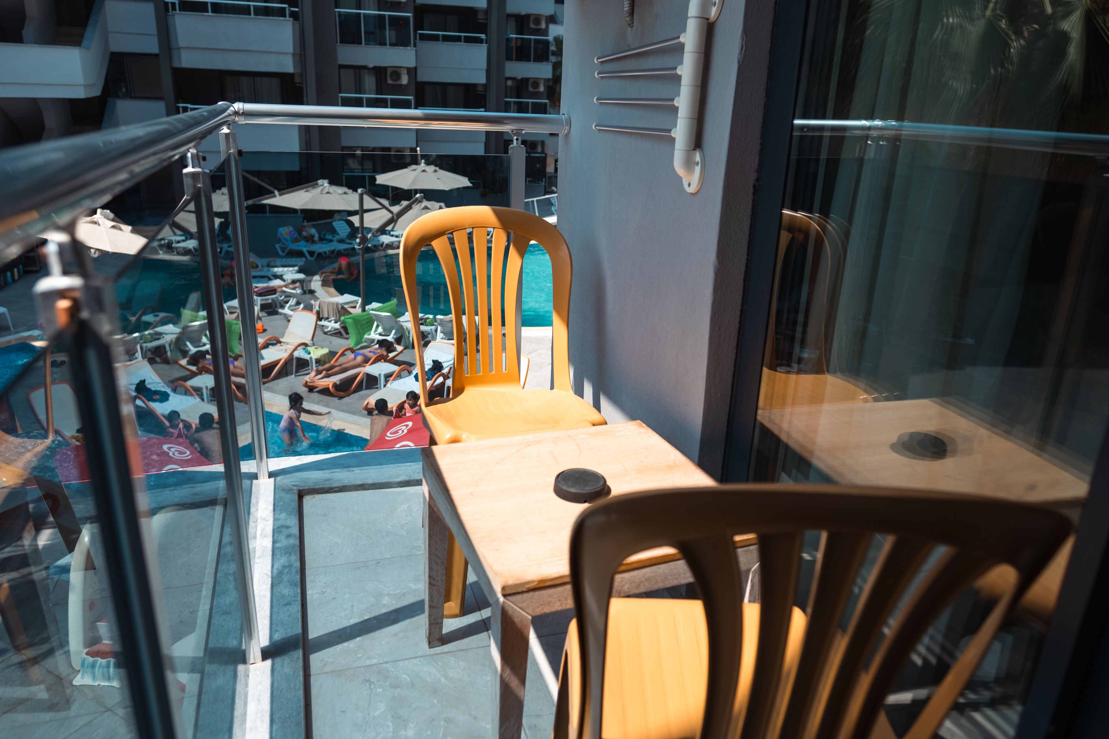 Varanda com guarda-corpo de vidro com vista para área de piscina com espreguiçadeiras e guarda-sóis.