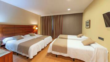 Quarto de hotel com duas camas de solteiro, cabeceira de madeira, escrivaninha com teclado e uma janela grande com cortinas.