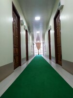 Um corredor longo com carpete verde, portas de madeira e uma luminária clara no teto.