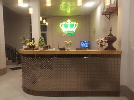 Bancada de recepção de hotel com logotipo de coroa, placa de recepção e plantas decorativas.