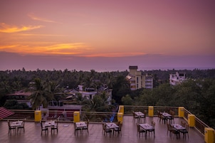 Terraço com mesas e cadeiras, com vista para um horizonte urbano com edifícios e palmeiras.