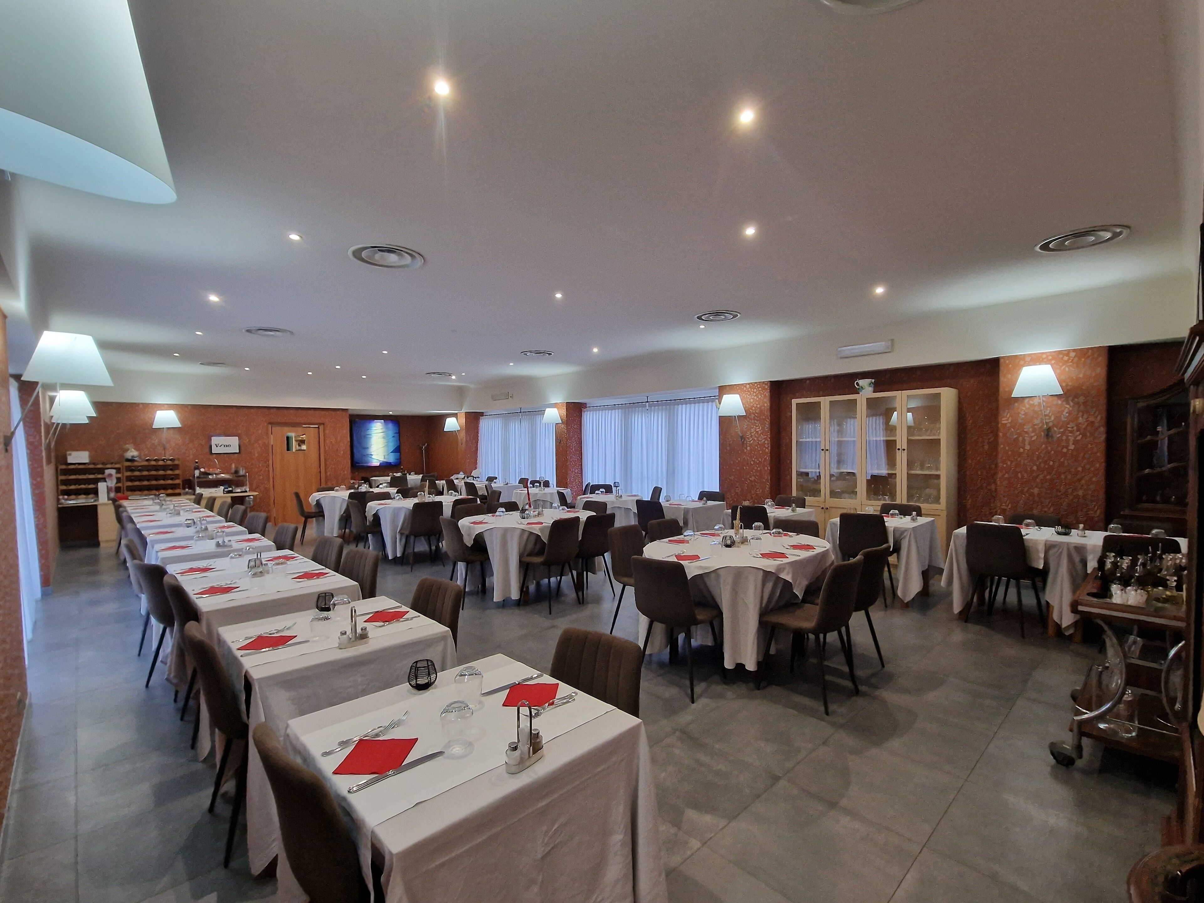 Uma sala de jantar de hotel com várias mesas redondas, cada uma com toalhas brancas, guardanapos vermelhos e talheres.