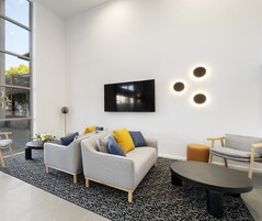 Uma sala de estar moderna com um sofá cinzento, almofadas amarelas e azuis, uma mesa de centro redonda e uma TV de tela plana fixada na parede.