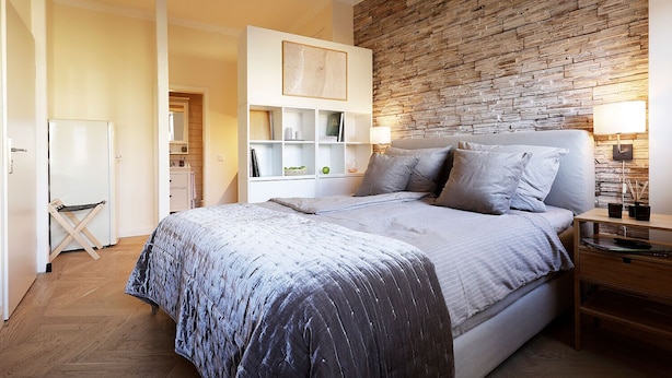 Quarto com cama, mesas de cabeceira, guarda-roupa e parede com padrão de tijolos.