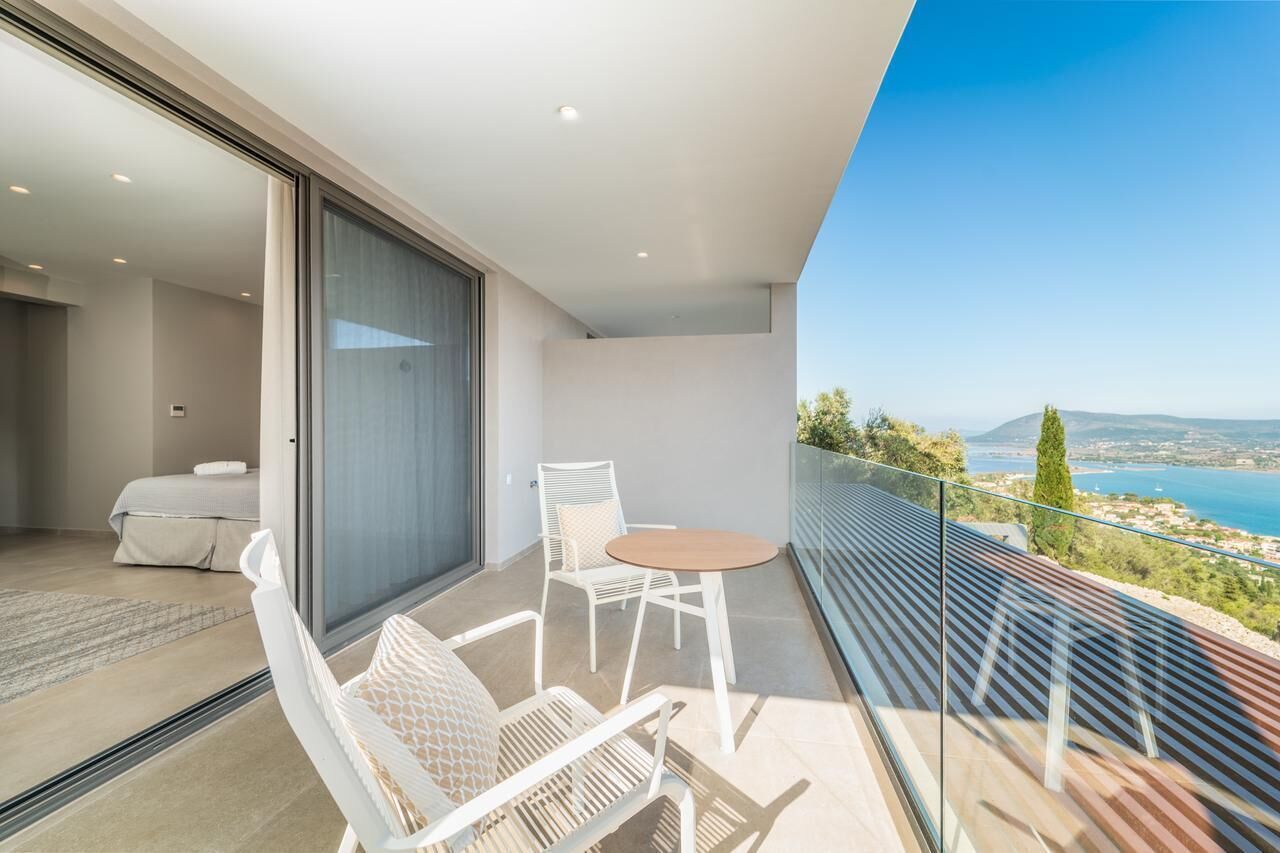 Varanda com vista para um corpo de água e colinas. Há uma cama e uma cadeira na varanda.
