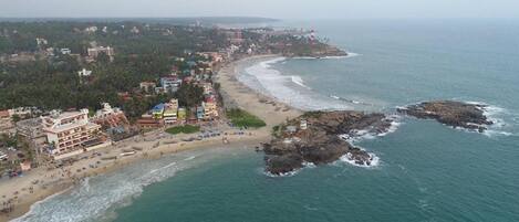 Vista aérea de uma área costeira com praia, afloramentos rochosos e um farol.