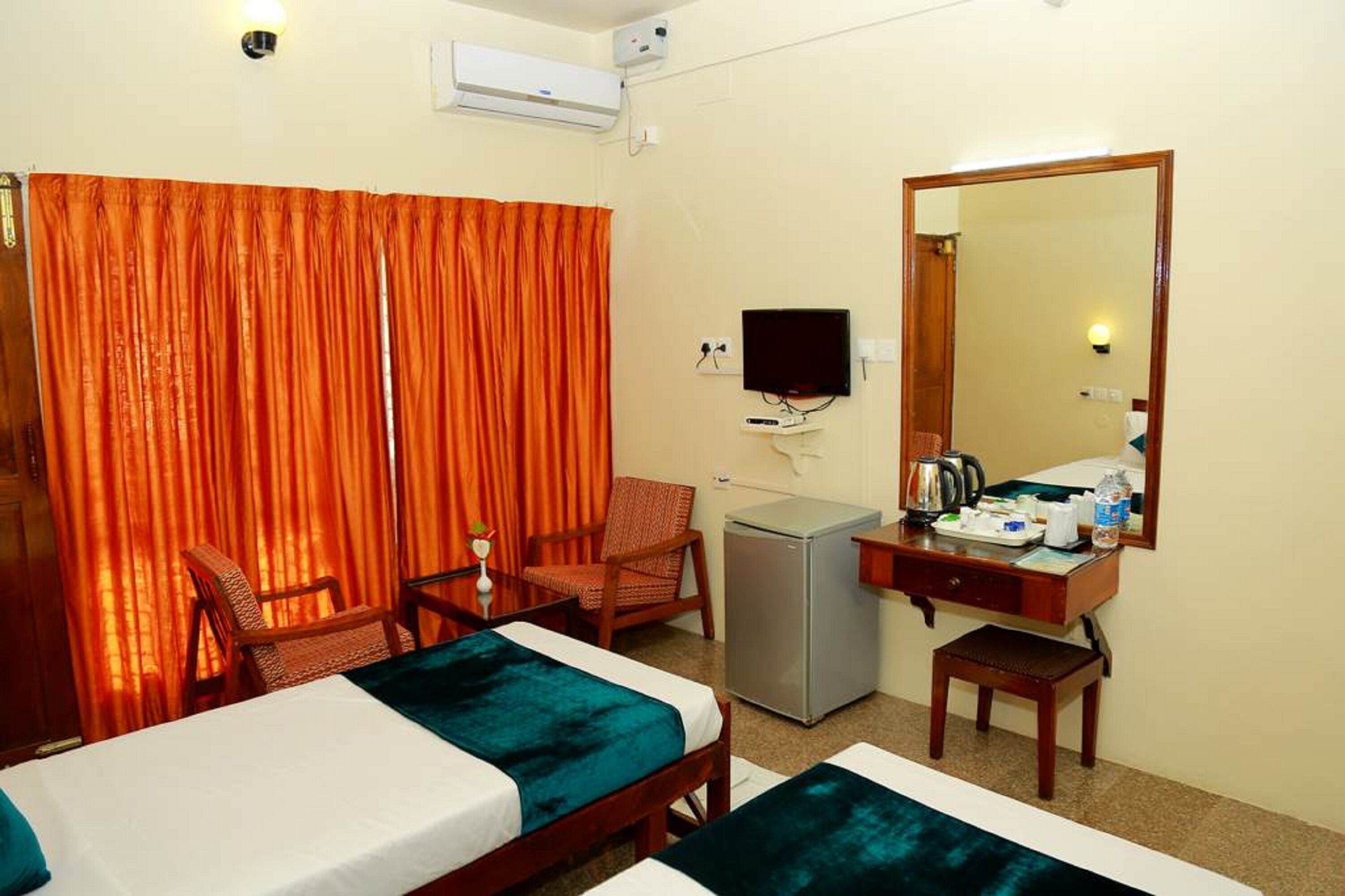 Quarto de hotel com duas camas, uma escrivaninha com espelho, televisão e frigorífico.