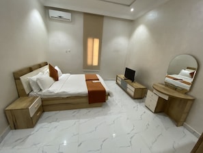 Quarto com cama, mesas de cabeceira, televisão, espelho e guarda-roupa.